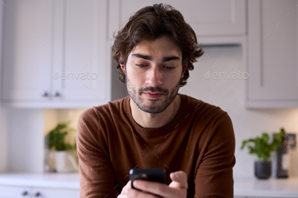 Young Man Relaxing At Home In Kitchen Checking Messages Social Media On ...