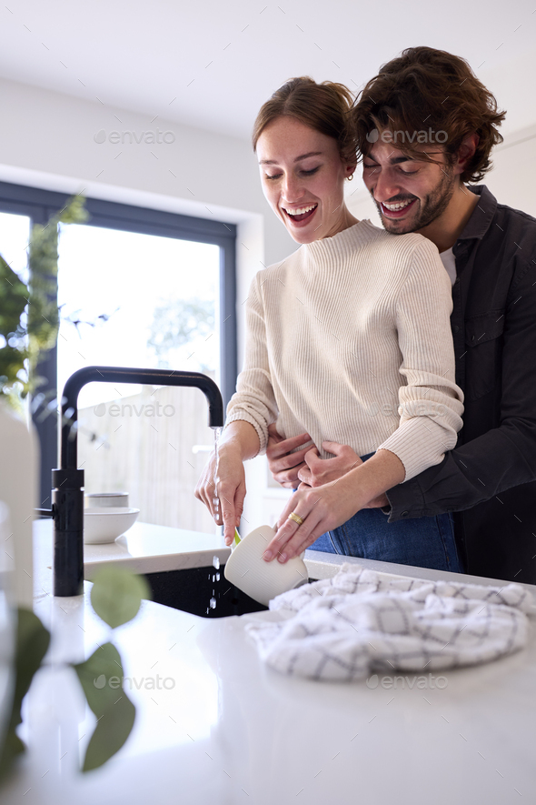 Couple Hugging At Home In Kitchen As Woman Does Washing Up Stock Photo ...