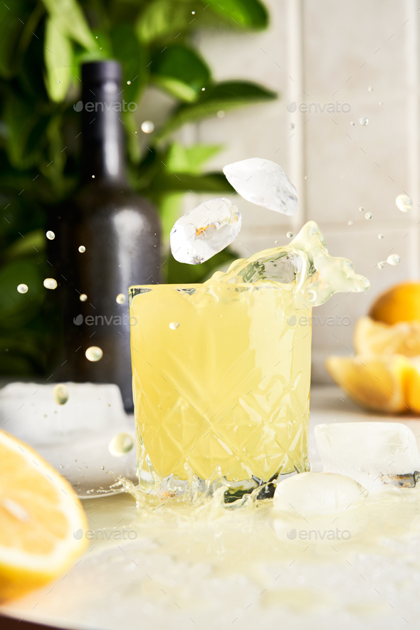 Ice falling on a traditional italian homemade lemon alcohol drink ...