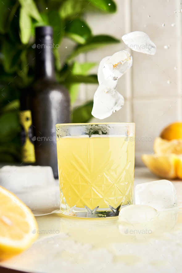 Ice falling on a traditional italian homemade lemon alcohol drink ...