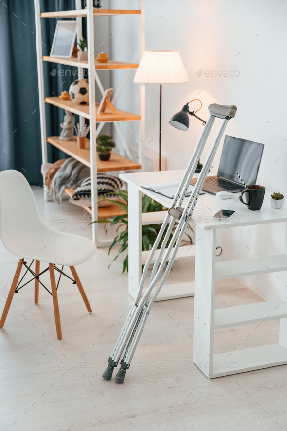 Crutches is leaning on the table in domestic room with laptop, chair ...