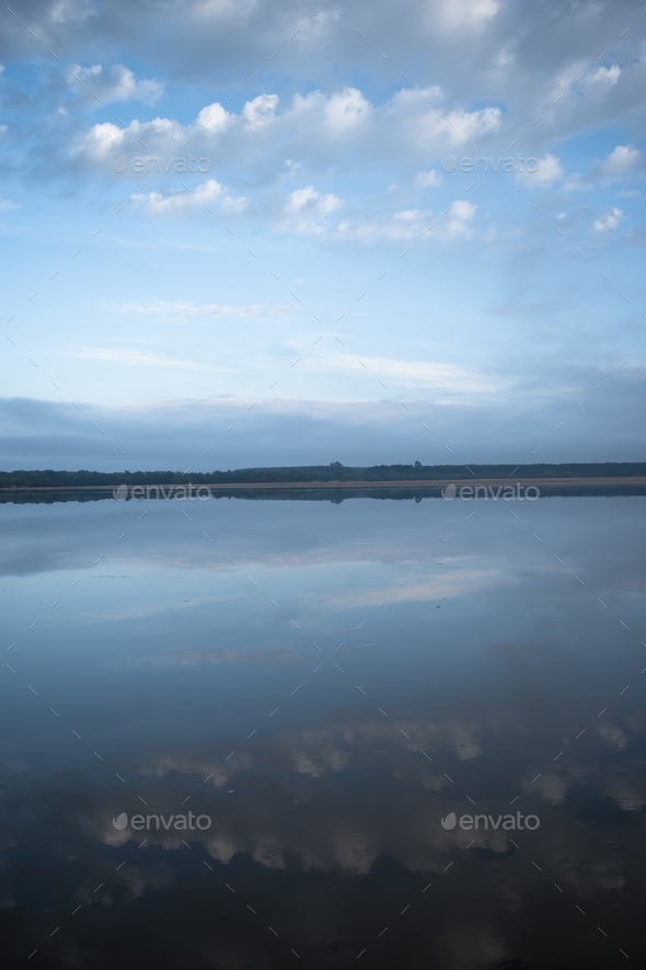 Vertical shot of a reflective lake surface on a cloudy sky background ...