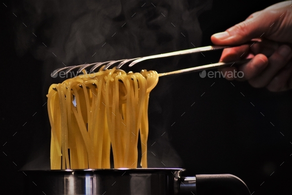 Closeup of a person holding hot pasta with a spaghetti tong with a dark ...