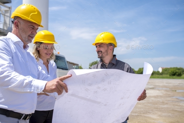 Group of construction workers looking at the plans and documents under ...