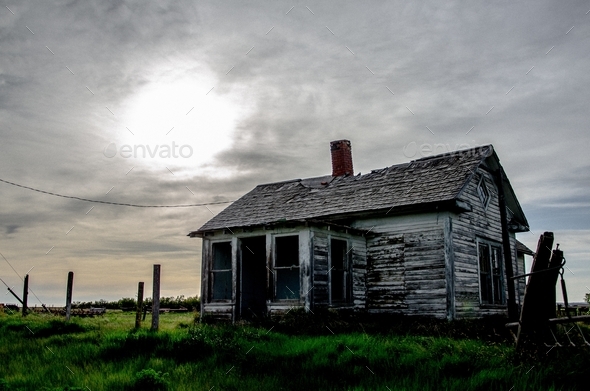 Creepy, old and aged abandoned house in a field under the cloudy and ...