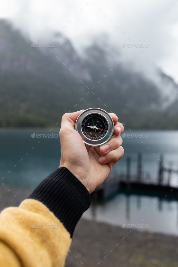 Human hand holding a compass and the lake surrounded with mountains in ...