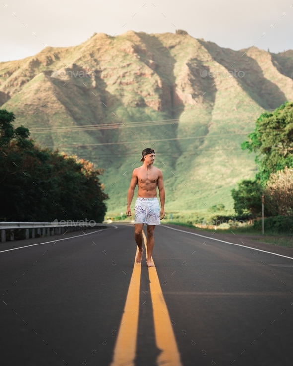 Vertical shot of a muscular fit man walking barefoot on an asphalt road ...