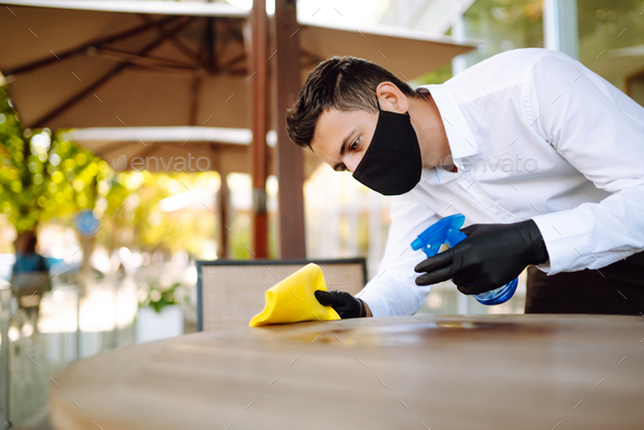 Disinfecting to prevent COVID-19. Waiter cleaning the table with ...