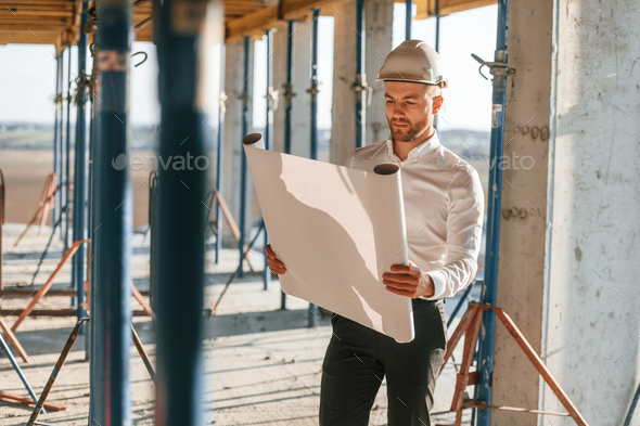 Holding plan in hands. Man is working on the construction site at ...