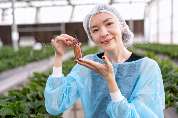 Doctor nutritionist in greenhouse farming proudly showing bottle of ...