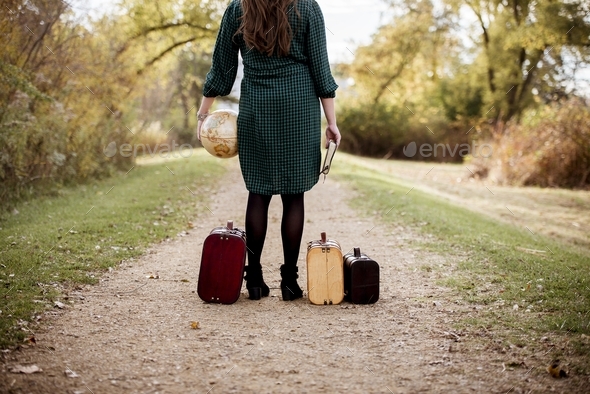 Female standing in between her old suitcases while holding a desk globe ...