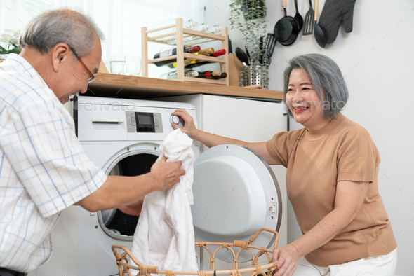 Happy Asian senior older man helping his wife put clothes in washing ...