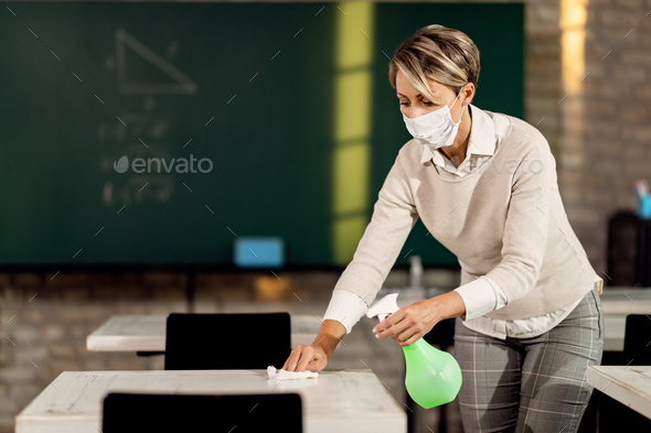 Female teacher disinfecting tables in the classroom during coronavirus ...