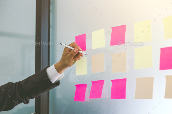 Close up hand businessman writing sticky notes on glass wall in office ...