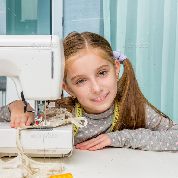 smiling little girl at the table with sewing machine Stock Photo by tan4ikk
