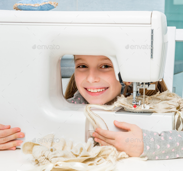 smiling little girl at the table with sewing machine Stock Photo by tan4ikk