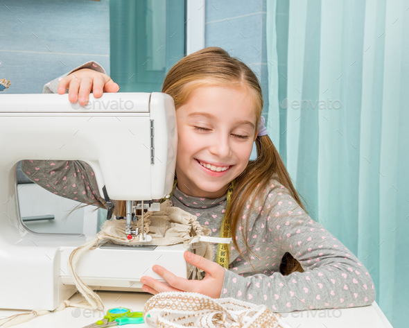 smiling little girl at the table with sewing machine Stock Photo by tan4ikk