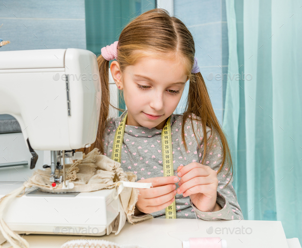smiling little girl at the table with sewing machine Stock Photo by tan4ikk