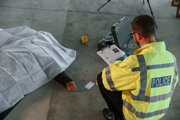 Male detective is collecting evidence in a crime scene near dead body on the construction site ...