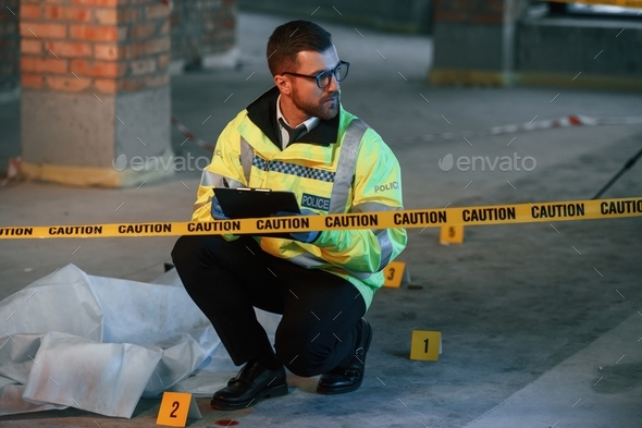 Male detective is collecting evidence in a crime scene near dead body on the construction site ...