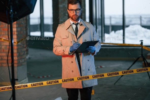 Male detective in coat is collecting evidence in a crime scene on the ...