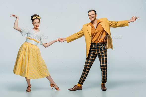 stylish dancers holding hands while dancing boogie-woogie on grey ...