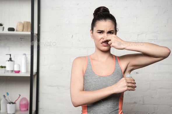 shocked woman plugging nose with hand while applying deodorant on ...