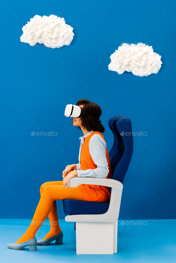 side view of african american in vr headset sitting on seat on blue ...