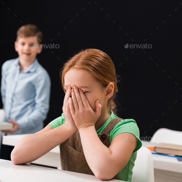 selective focus of upset kid crying near classmate isolated on black ...