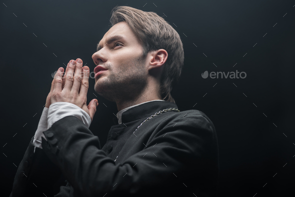 low angle veiw of young concentrated catholic priest praying isolated ...