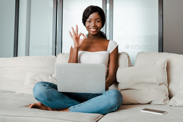 African american freelancer with crossed legs and laptop smiling and ...