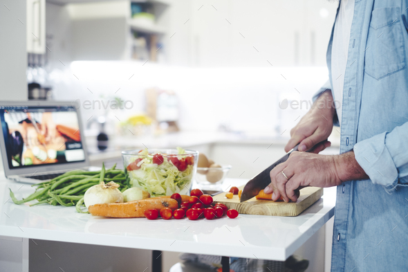 One man watching video recipe on laptop while cooking vegetables in ...