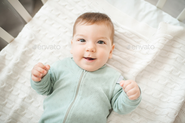 Smiling newborn baby wake up in bed close up Stock Photo by morrowlight
