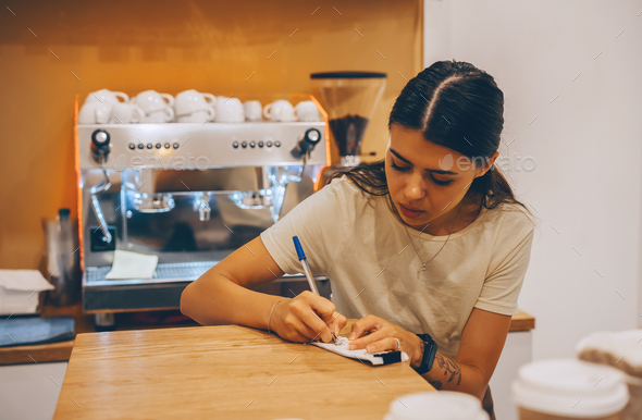 Young female waitress barista checking bills and receipts, taking notes ...