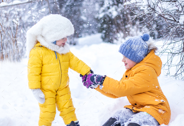 little girl in yellow snowsuit giving helping hand to boy in yellow ...