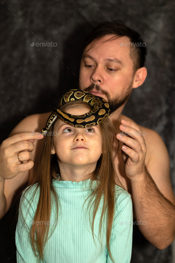 Father and daughter playing with snake. Portrait of smiling girl in ...