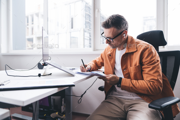 Focused man writing notes in papers at workplace Stock Photo by GaudiLab