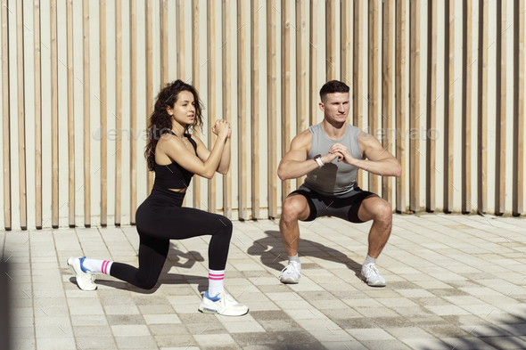 Two fit young people bending knees to full squat position Stock Photo ...