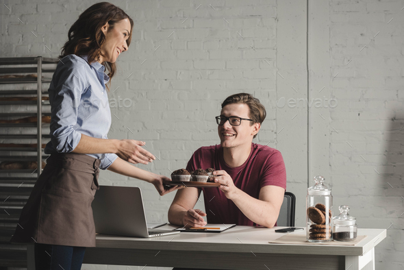 Smiling male and female bakers talking and examining pastries in bakery ...