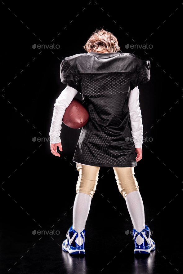 Back view of little boy american football player standing with ball on ...