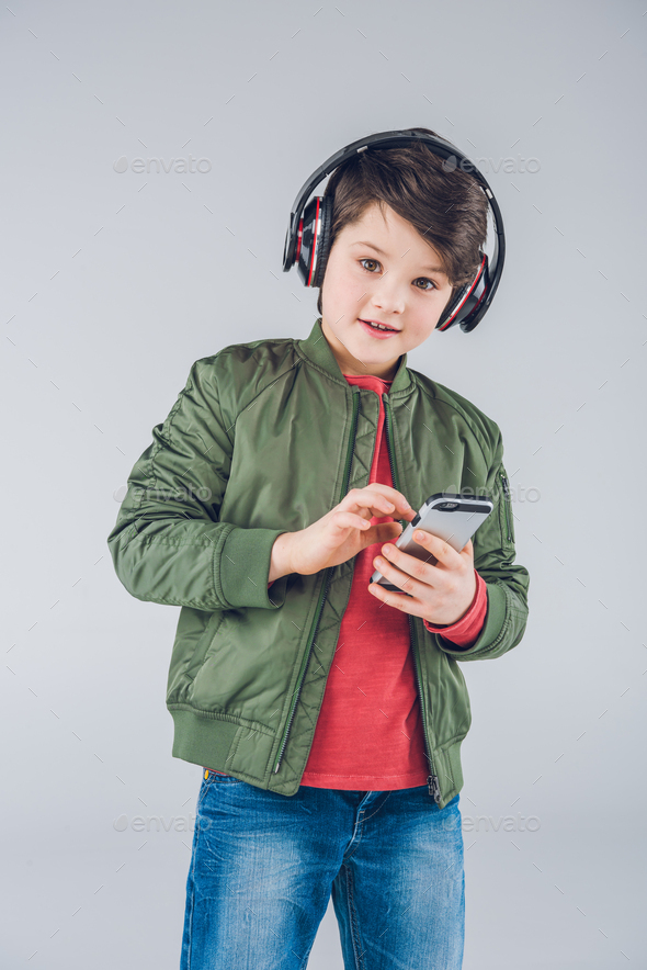 Cute boy with headphones and smartphone looking at camera isolated on ...