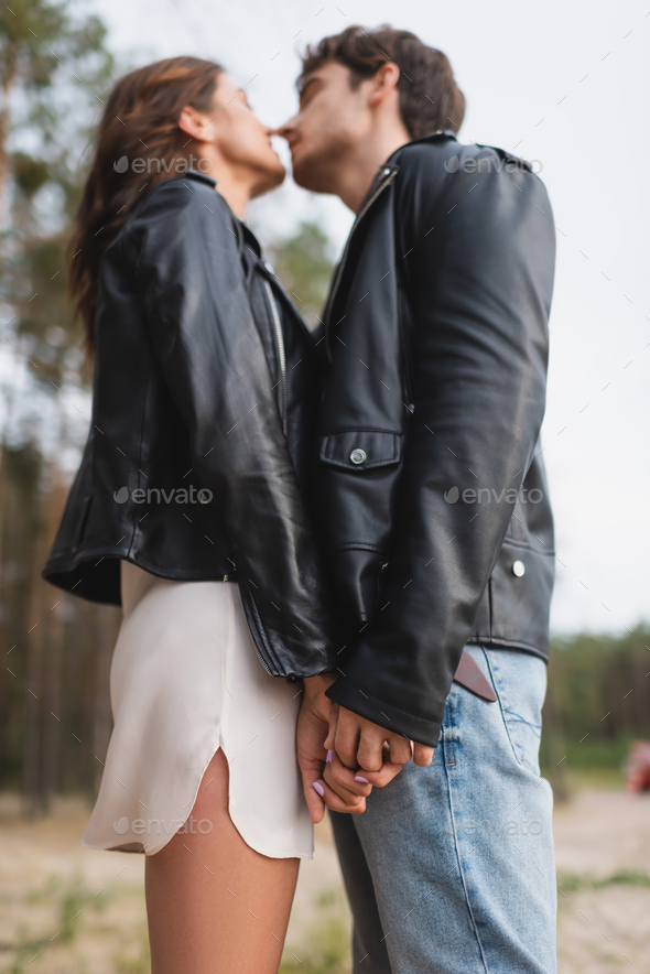 Low angle view of young couple in leather jackets holding hands and kissing in forest Stock ...