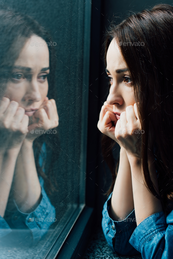 sad brunette woman touching face while looking at window Stock Photo by ...