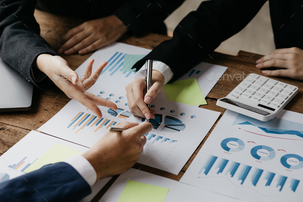 A group of people pointing to papers on a table in a conference room ...