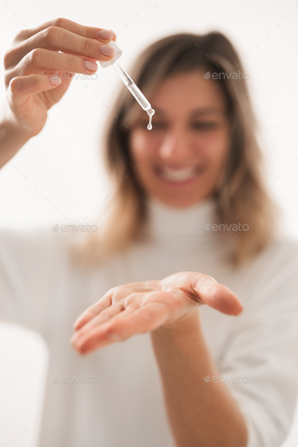 Cheerful young woman applying serum on hand and smiling Stock Photo by ...
