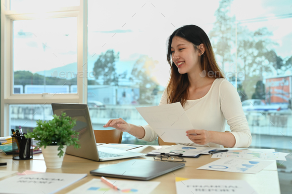 Pleasant young female employee using laptop computer and checking ...