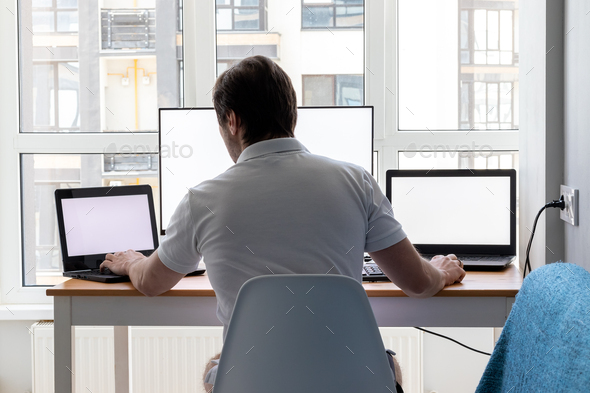 Man at workplace with two laptops and monitor. Remote work from home ...