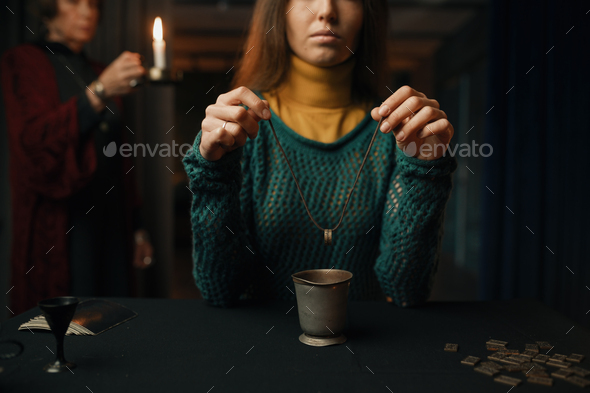Woman making divination with ring under mature professional gypsy ...