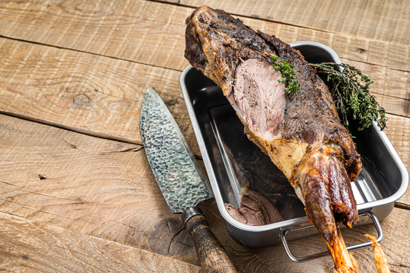 Whole oven roasted goat leg meat with thyme in a steel tray. Wooden ...