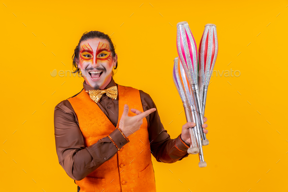 Portrait of a happy juggler man in make up vest juggling with maces on ...
